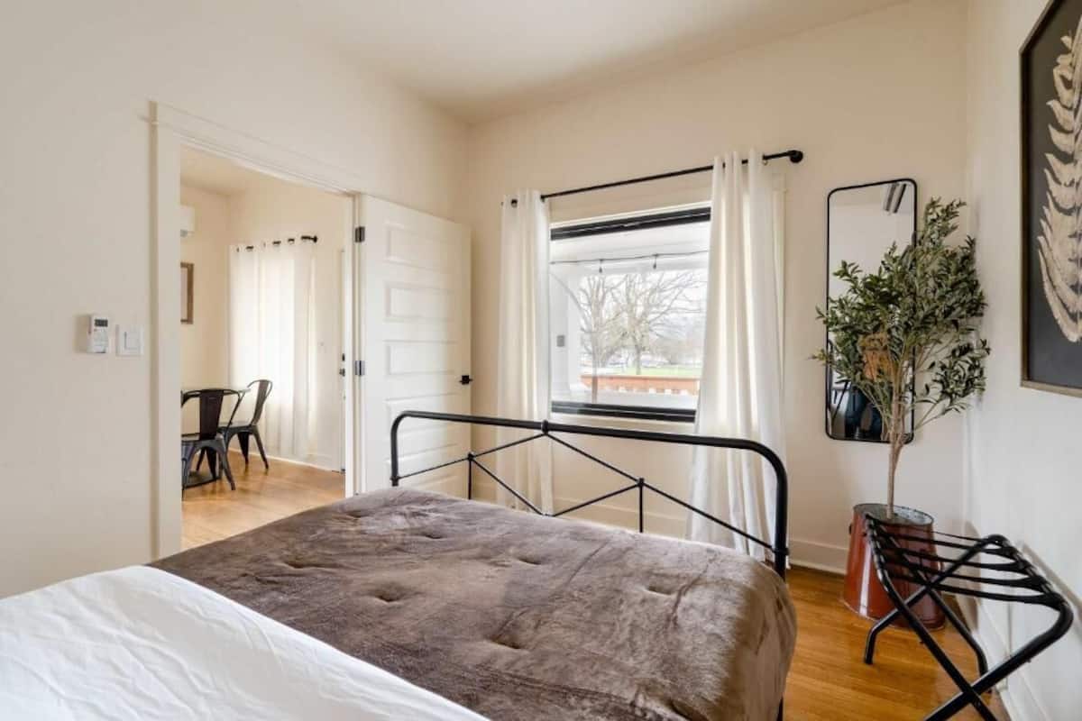 Quarto com cama, janela com cortinas, planta em vaso e uma cadeira.