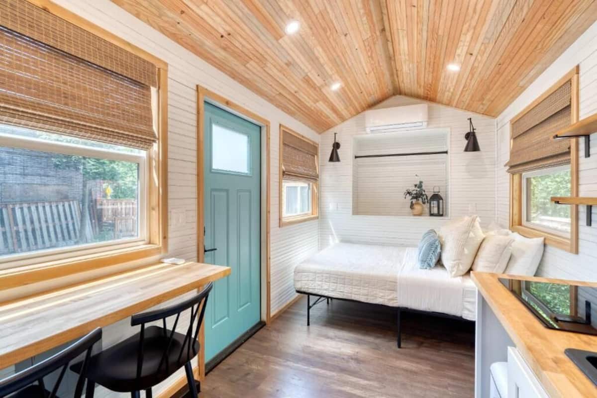 Quarto compacto com cama, mesa e cadeiras, paredes de madeira e teto inclinado.