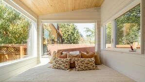 Quarto com cama grande, várias almofadas, teto de madeira e janelas amplas.