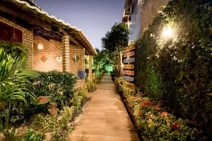 Um caminho ladeado por vegetação exuberante e um edifício de tijolos com telhado em cerâmica.