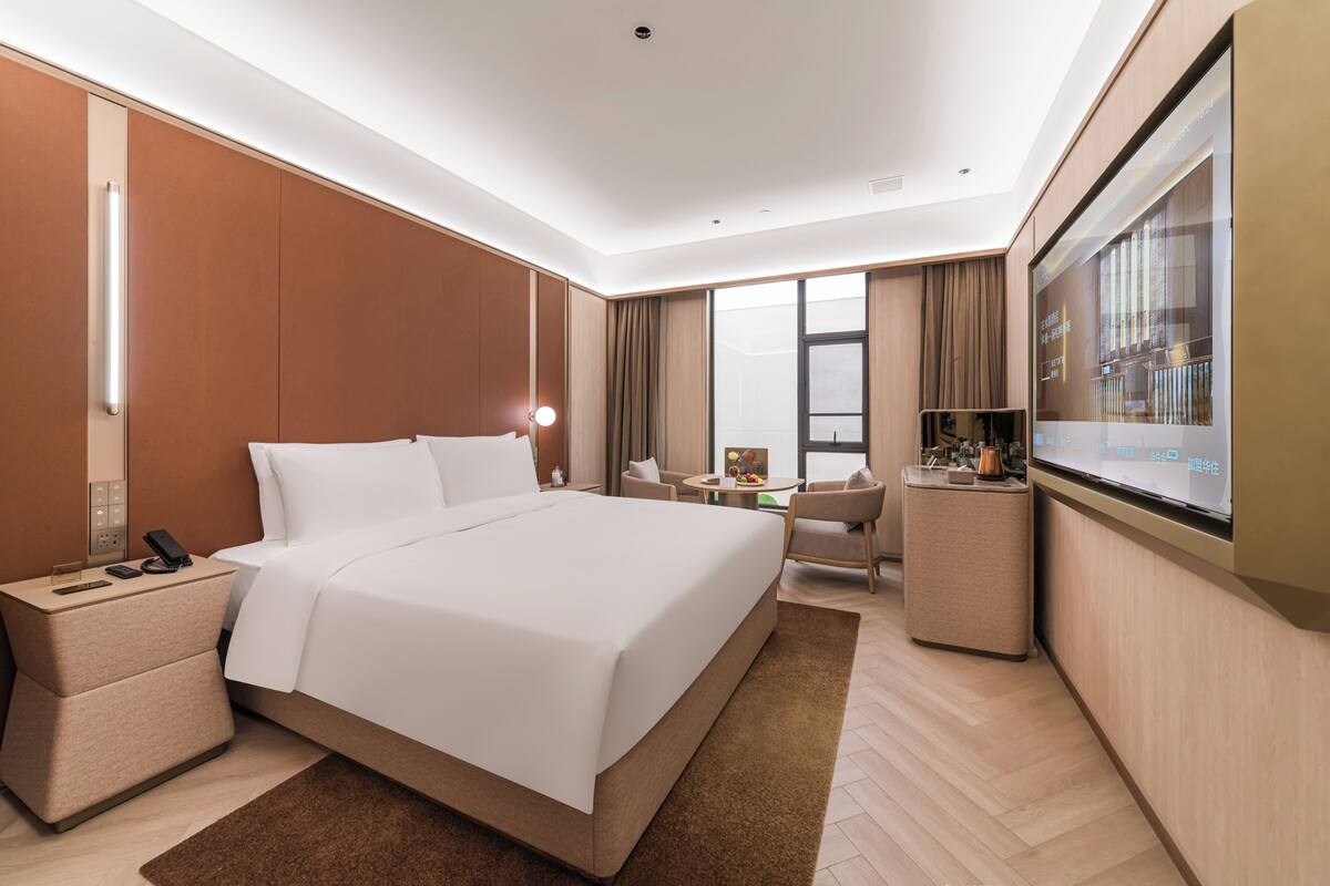 Quarto de hotel moderno com uma cama grande, mesas de cabeceira, escrivaninha e televisão.