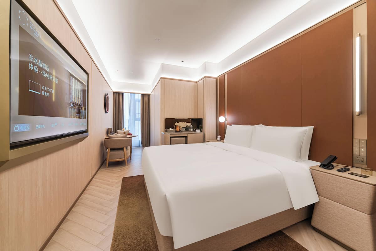 Quarto de hotel com cama, mesa de cabeceira, televisão, escrivaninha, cadeira e vista para o exterior.