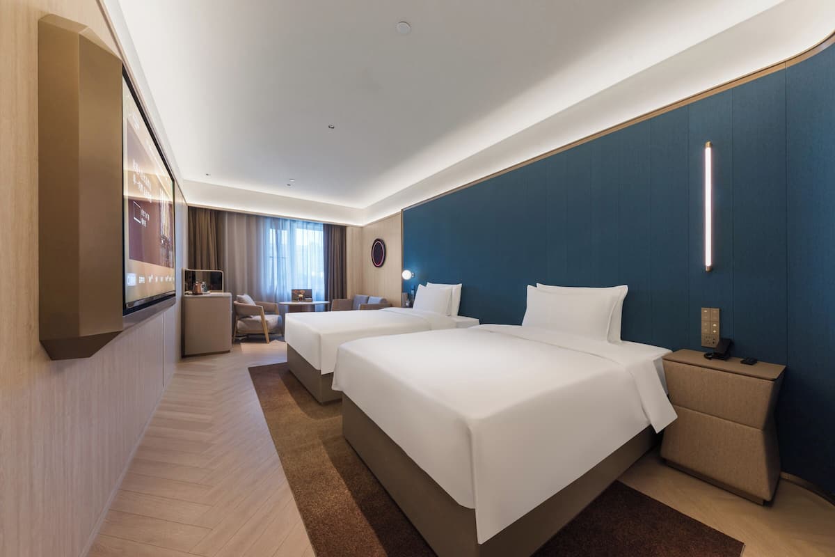 Quarto de hotel com duas camas, televisão de tela plana, escrivaninha e mesa de cabeceira.