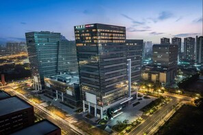 Um hotel moderno com fachada de vidro, vários andares e uma sinalização chamativa.