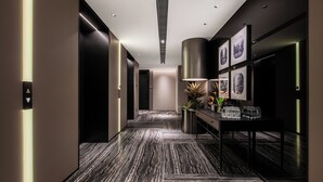 Um corredor moderno com piso de mármore, um balcão de recepção com uma planta, quadros emoldurados e um luminário fixado na parede.