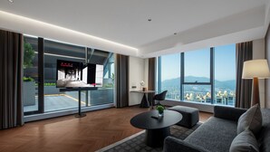 Quarto de hotel moderno com uma grande janela, uma mesa redonda, um sofá e uma pequena mesa com uma cadeira.