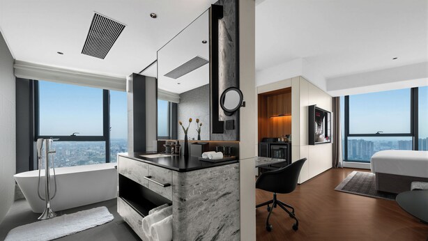 Quarto de hotel moderno com uma janela grande, toucador de mármore, cadeira de escritório preta e uma cama.