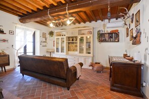 Um interior rústico com vigas de madeira aparentes, um sofá de couro marrom, uma mesa de jantar com abajur e um armário com portas de vidro.