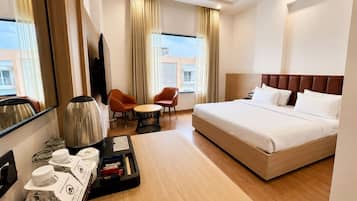 Quarto de hotel com cama, escrivaninha com cafeteira, uma cadeira e janela com cortinas.