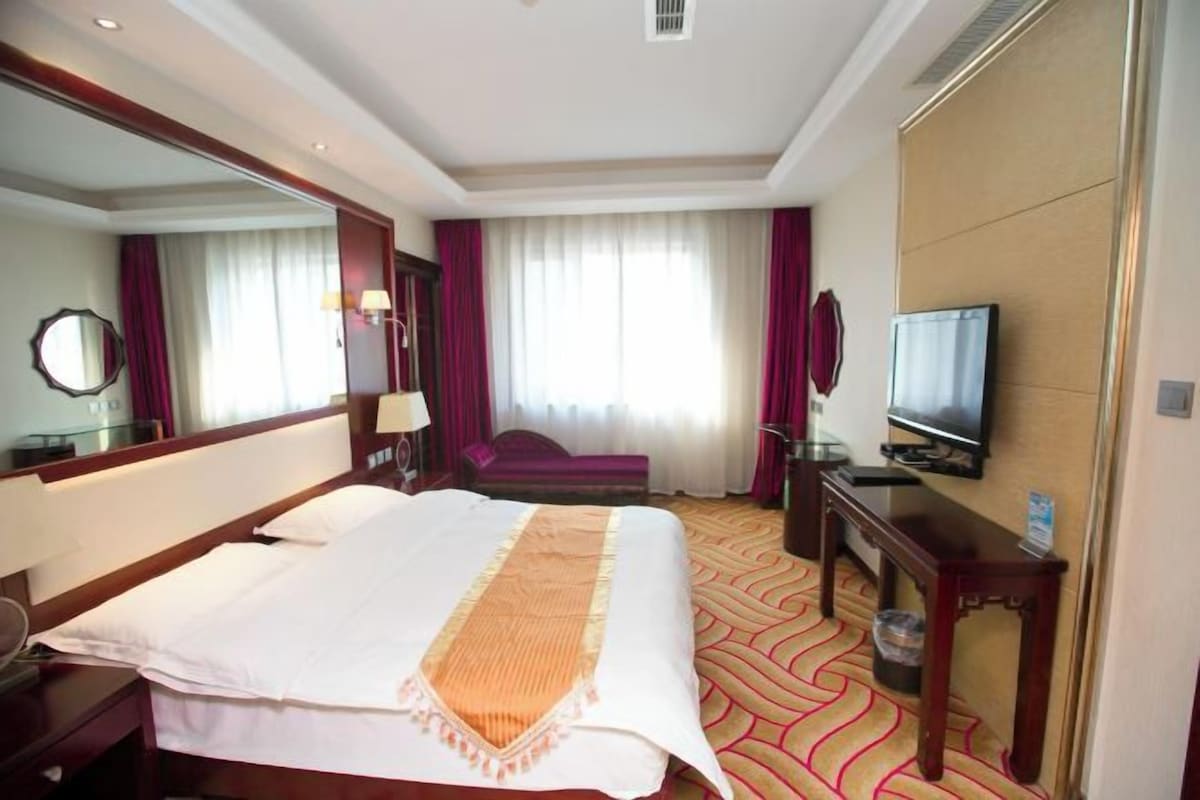 Quarto de hotel com uma cama, televisão, escrivaninha e janela com cortinas.