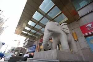 Uma grande estátua de elefante em frente a um edifício com teto de vidro e uma placa com caracteres chineses.