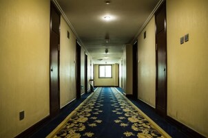 Corredor de hotel com piso em carpete, portas em ambos os lados e uma janela no final.