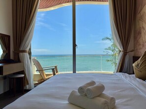 Quarto de hotel com cama, escrivaninha, cadeira e vista para o mar.