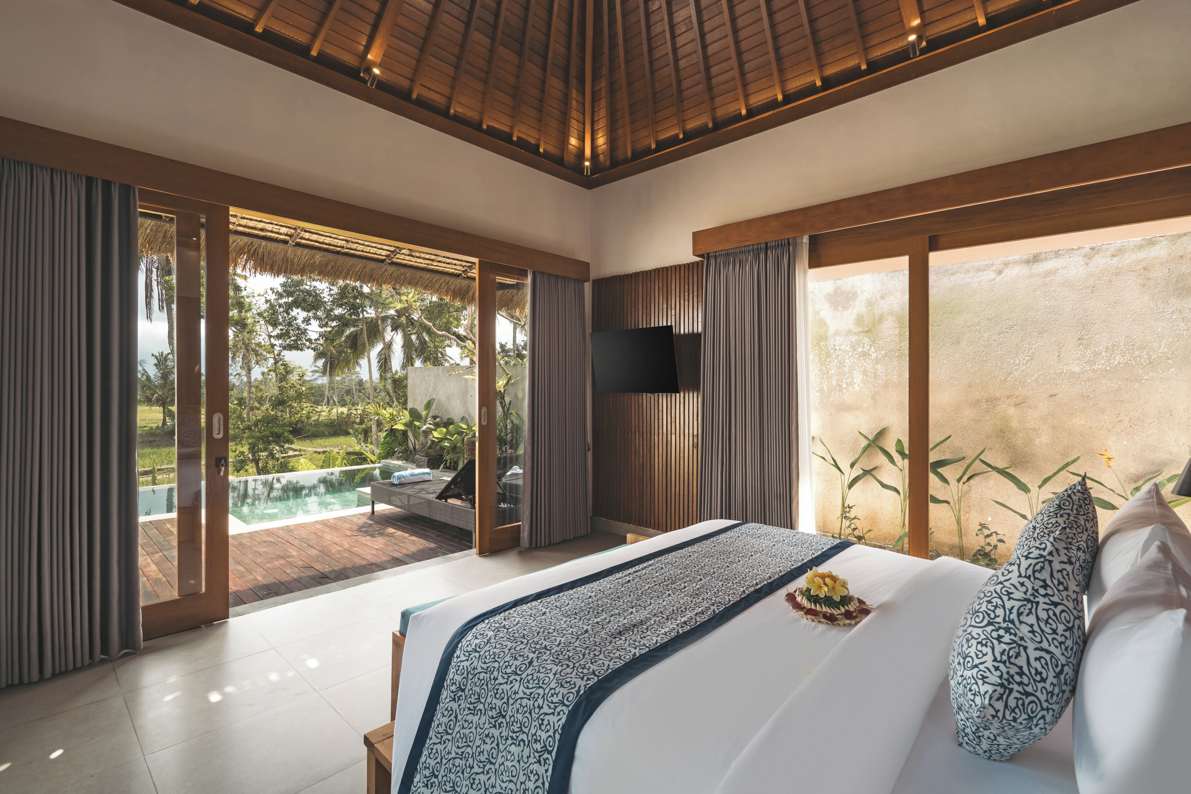 Quarto com uma cama grande, televisão e vista para a piscina e jardim.