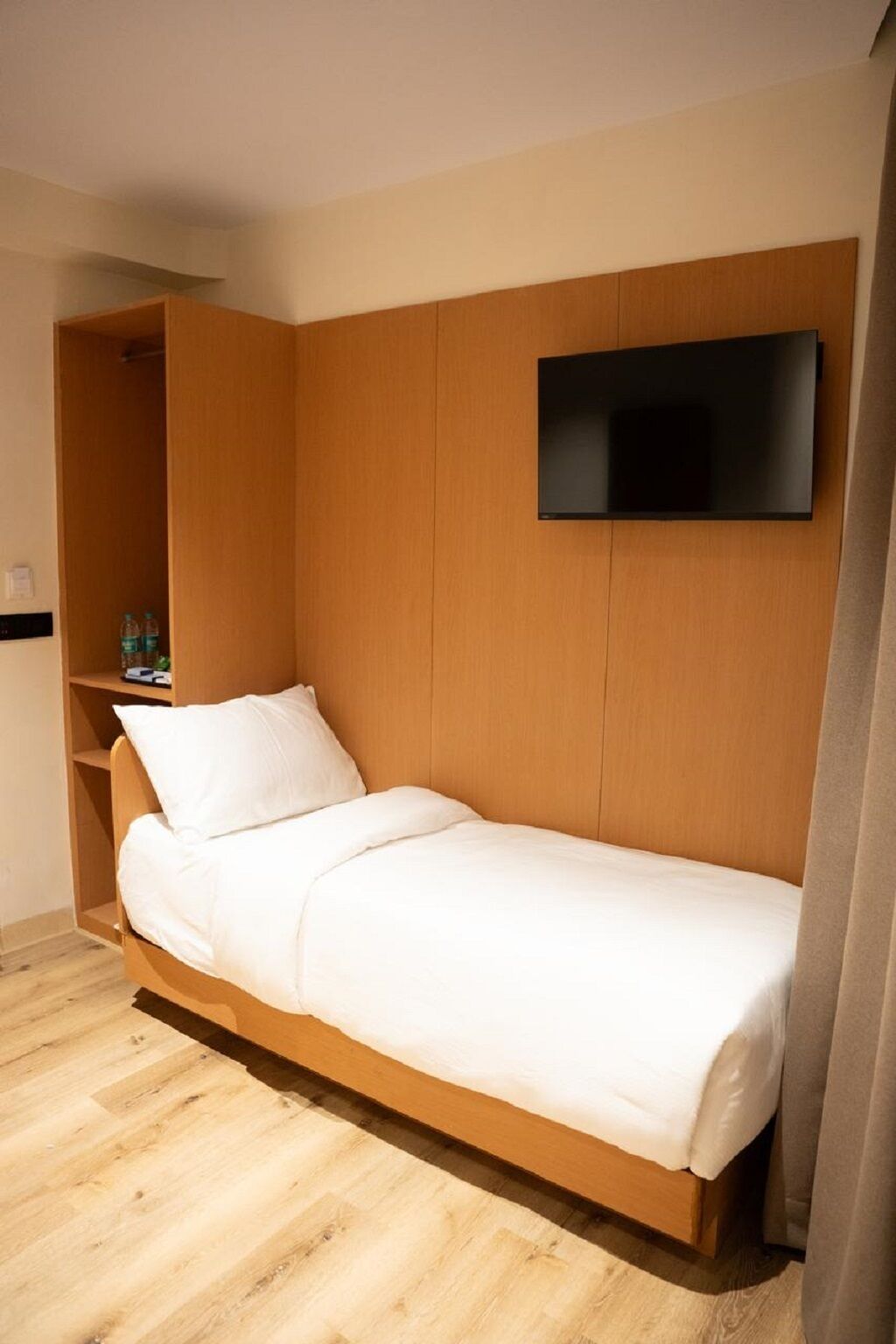 Uma cama de solteiro com cabeceira de madeira, uma televisão de tela plana na parede e um guarda-roupa de madeira com uma prateleira.