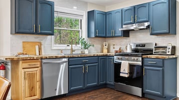 Cozinha moderna com armários azul escuro, eletrodomésticos de aço inoxidável e janela com vista para vegetação.