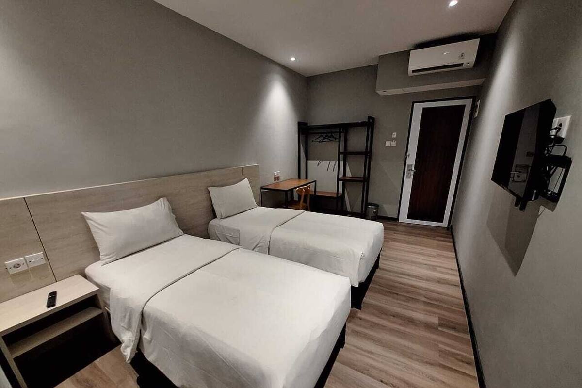 Quarto de hotel com duas camas, uma mesa pequena, uma cadeira, televisão e ar condicionado.