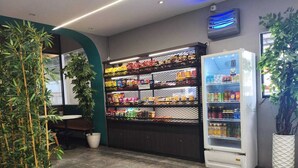 Máquina automática de vendas, uma prateleira com lanches e uma planta em vaso num quarto.