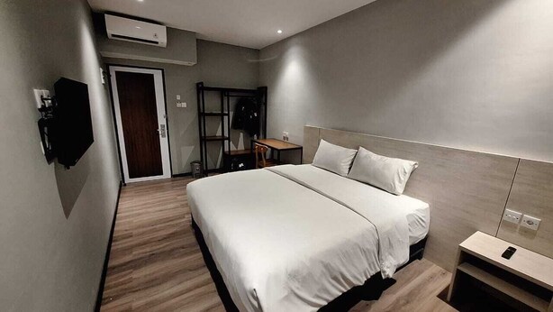 Quarto de hotel moderno com uma cama grande, mesa de cabeceira, escrivaninha e ar condicionado.