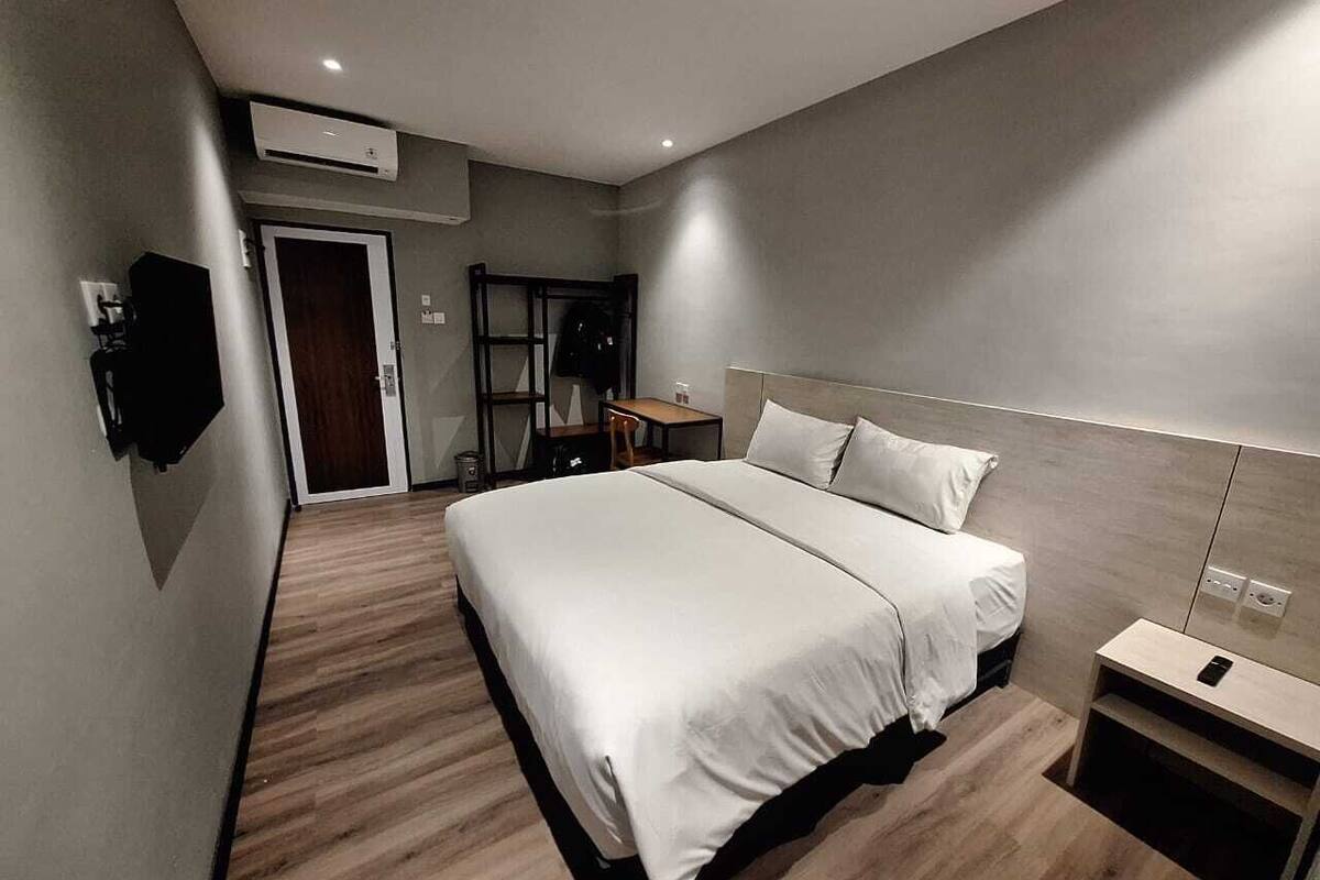 Quarto de hotel moderno com uma cama grande, mesa de cabeceira, escrivaninha e ar condicionado.