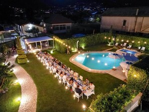 Área de refeições ao ar livre com piscina, cercada por vegetação e céu noturno limpo.