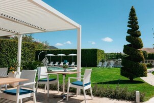 Área de estar coberta ao ar livre, com piscina, espreguiçadeiras e um jardim bem cuidado.
