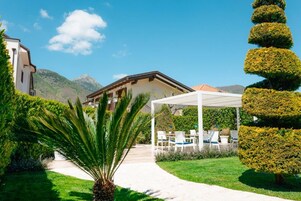 Um jardim com um caminho que leva a uma área coberta com cadeiras e mesas.