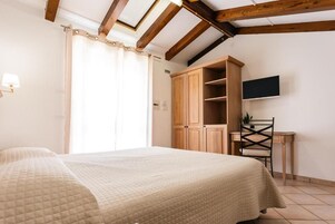 Quarto com cama, escrivaninha, cadeira, guarda-roupa e televisão na parede.