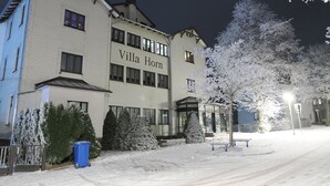 Um edifício chamado 'Villa Horn' com fachada coberta de neve, entrada com portão e uma lixeira à vista.