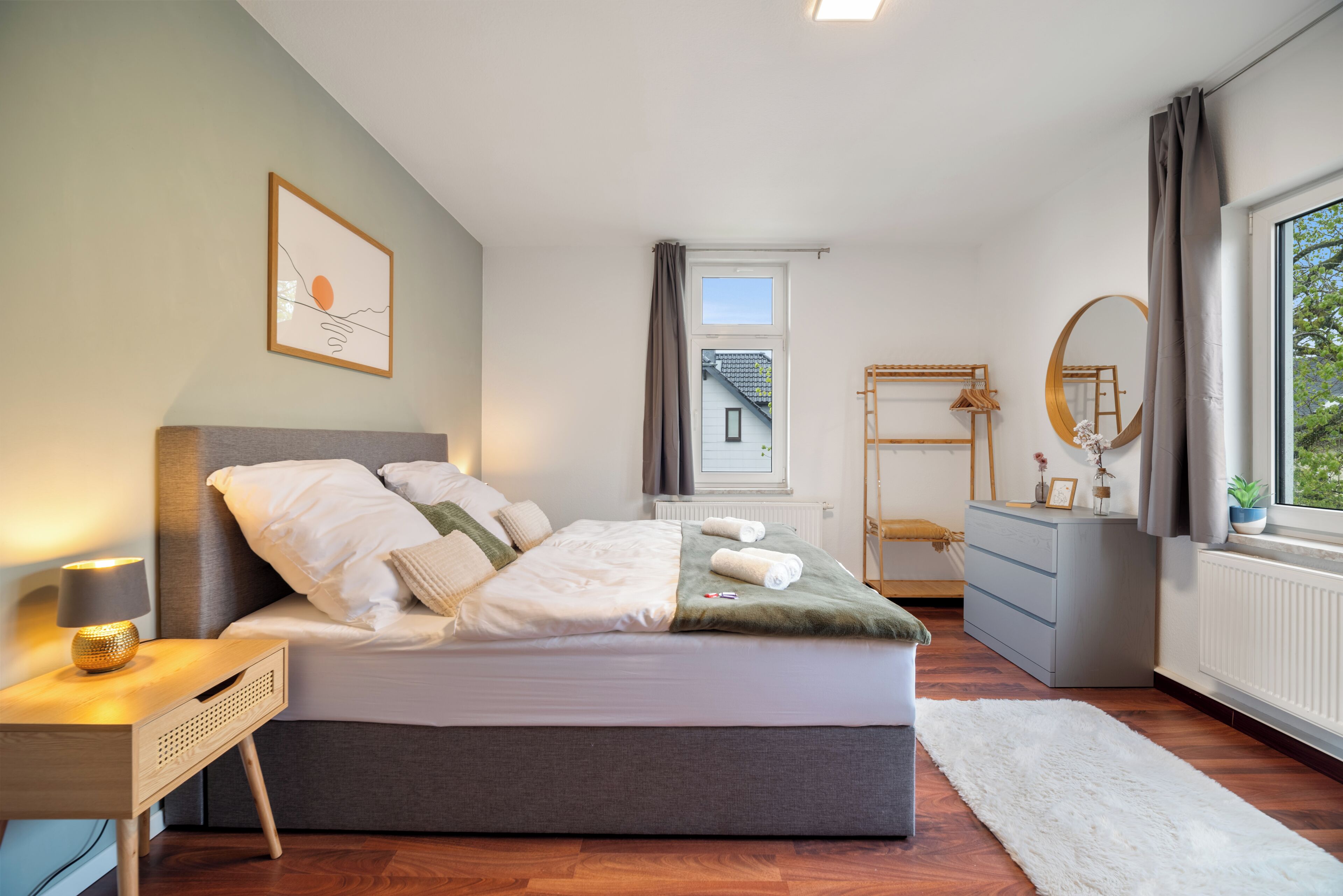 Quarto com cama, mesa de cabeceira, penteadeira, espelho e janela.