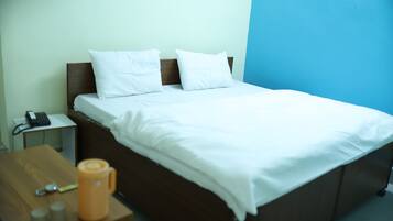 Uma cama de solteiro com roupa de cama branca, cabeceira de madeira, mesa de cabeceira com um telefone e uma caneca, e parede azul.