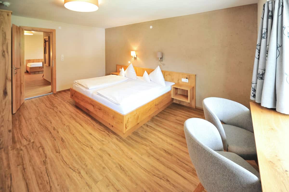 Quarto com cama de madeira, mesa de cabeceira, uma cadeira e piso de madeira.