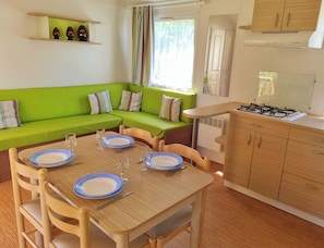 Um espaço de estar compacto com um sofá verde, uma mesa de jantar para quatro pessoas e uma cozinha compacta com fogão.