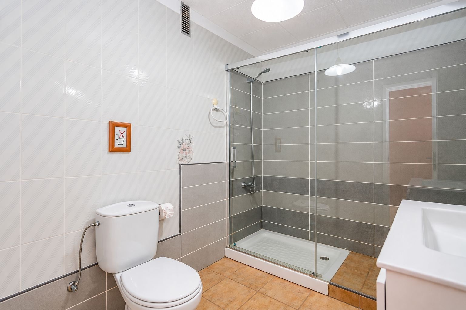 Uma casa de banho moderna com sanita, chuveiro e lavatório.