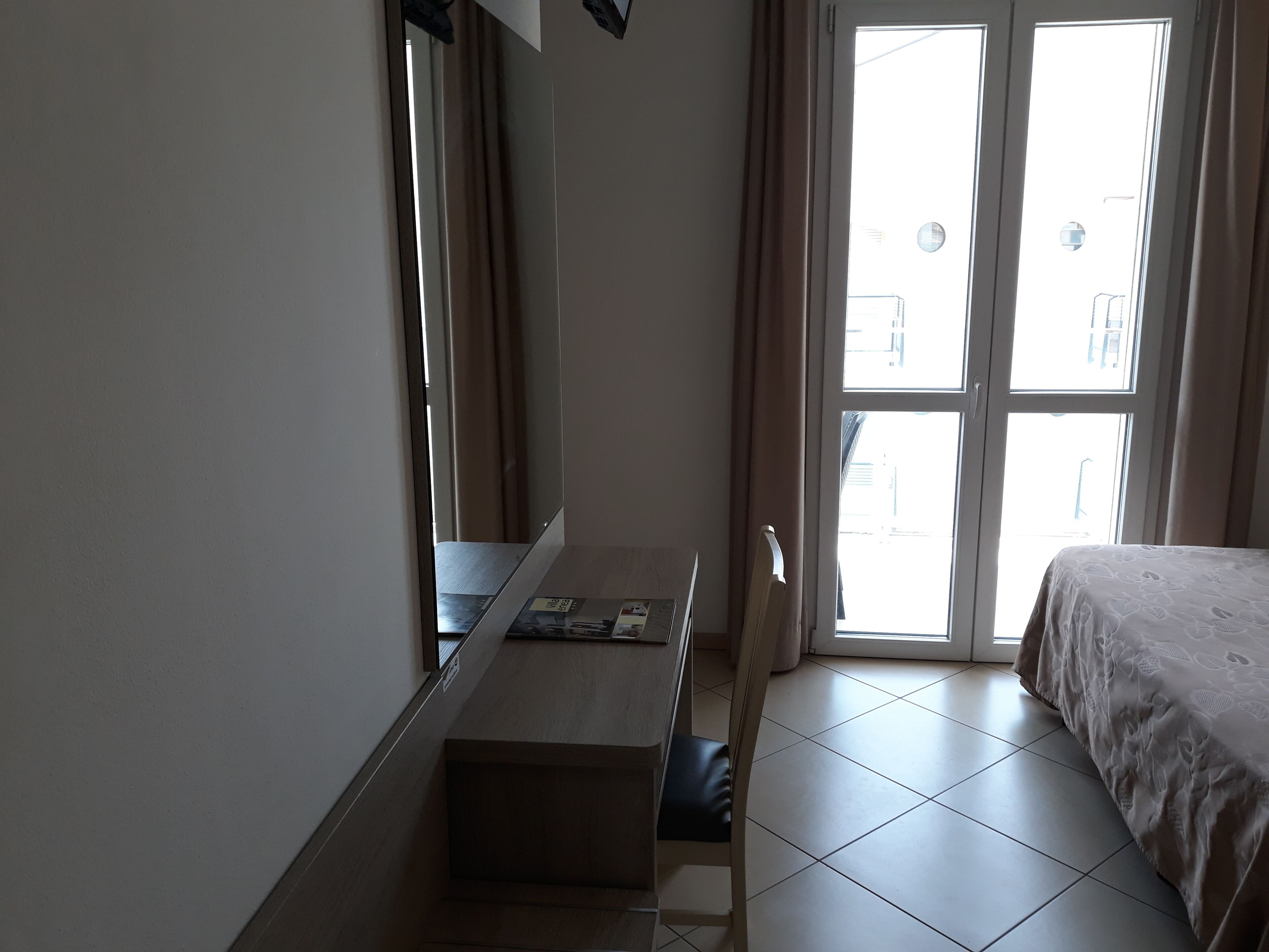 Quarto com cama, escrivaninha, cadeira e janela com cortinas.