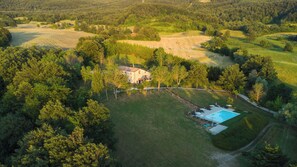 Vista aérea de uma propriedade rural com uma casa de pedra, piscina e campos ao redor.