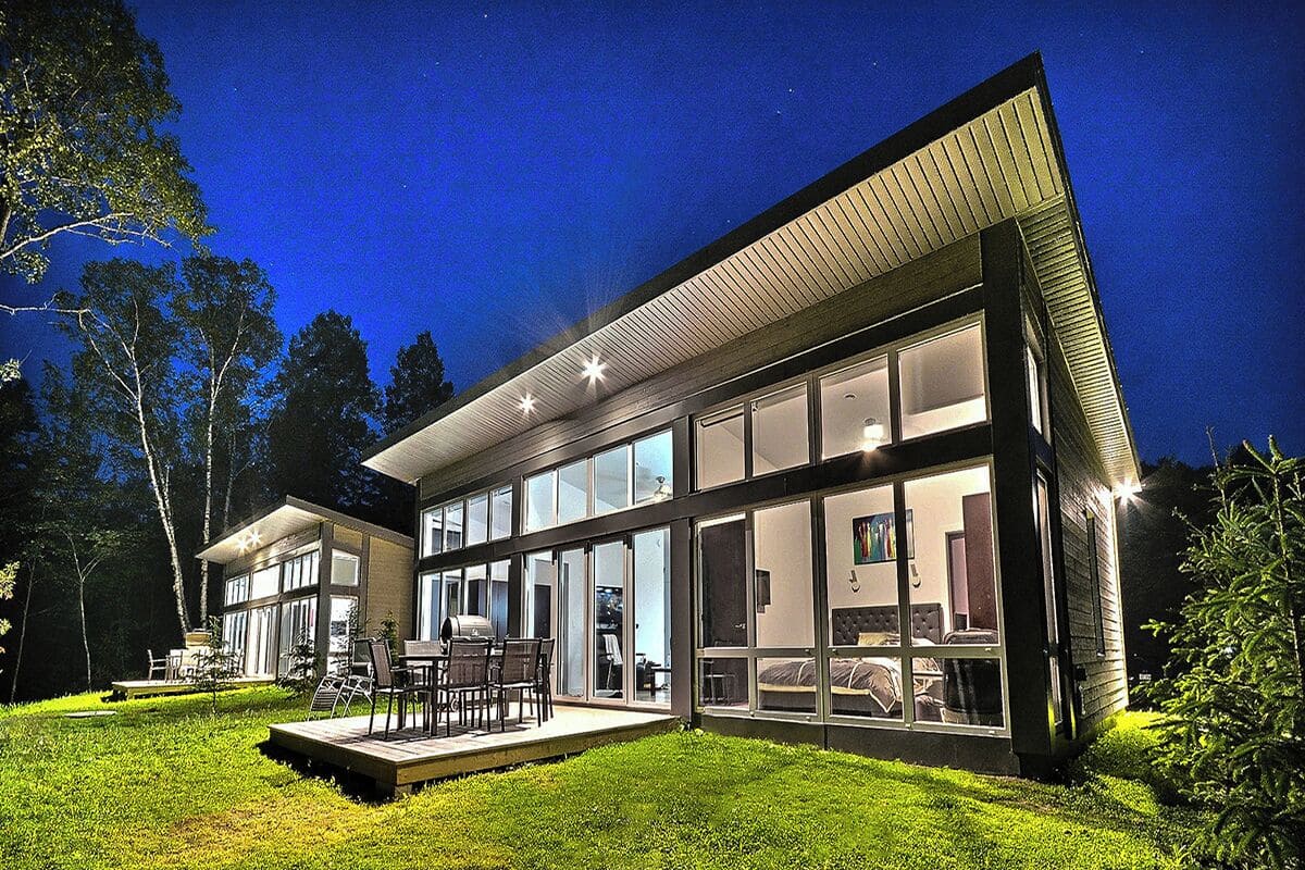 Uma casa moderna com amplas janelas de vidro, um pátio com móveis de exterior e interior bem iluminado.