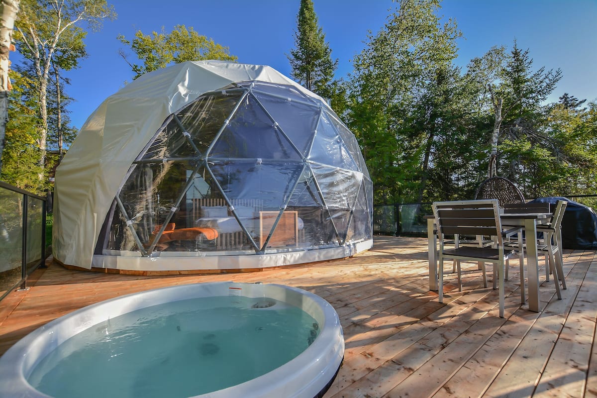 Estrutura em cúpula geodésica com hidromassagem e mobiliário exterior em um deck de madeira.