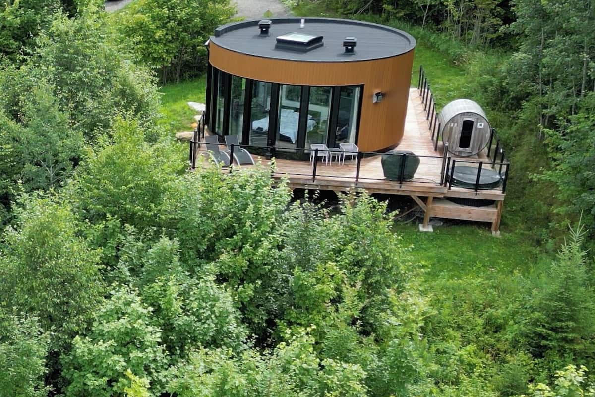 Uma cabana circular de madeira com paredes de vidro, um deck e uma sauna.