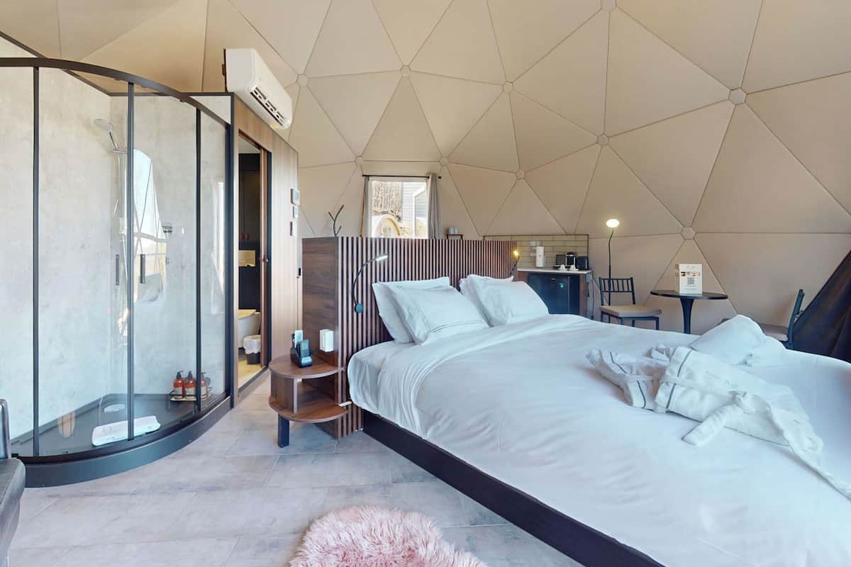 Quarto moderno com cama grande, chuveiro em gabinete de vidro e uma kitchenette.