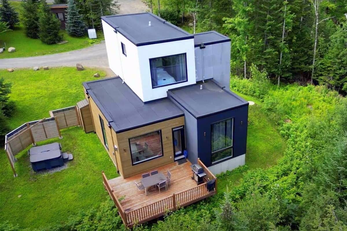Uma casa moderna de dois andares com varanda, uma pequena área de estar externa e uma grande janela.