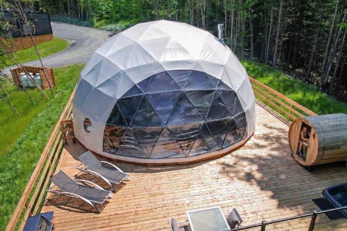 Uma estrutura em forma de cúpula geodésica com terraço, espreguiçadeiras e banheira de hidromassagem.
