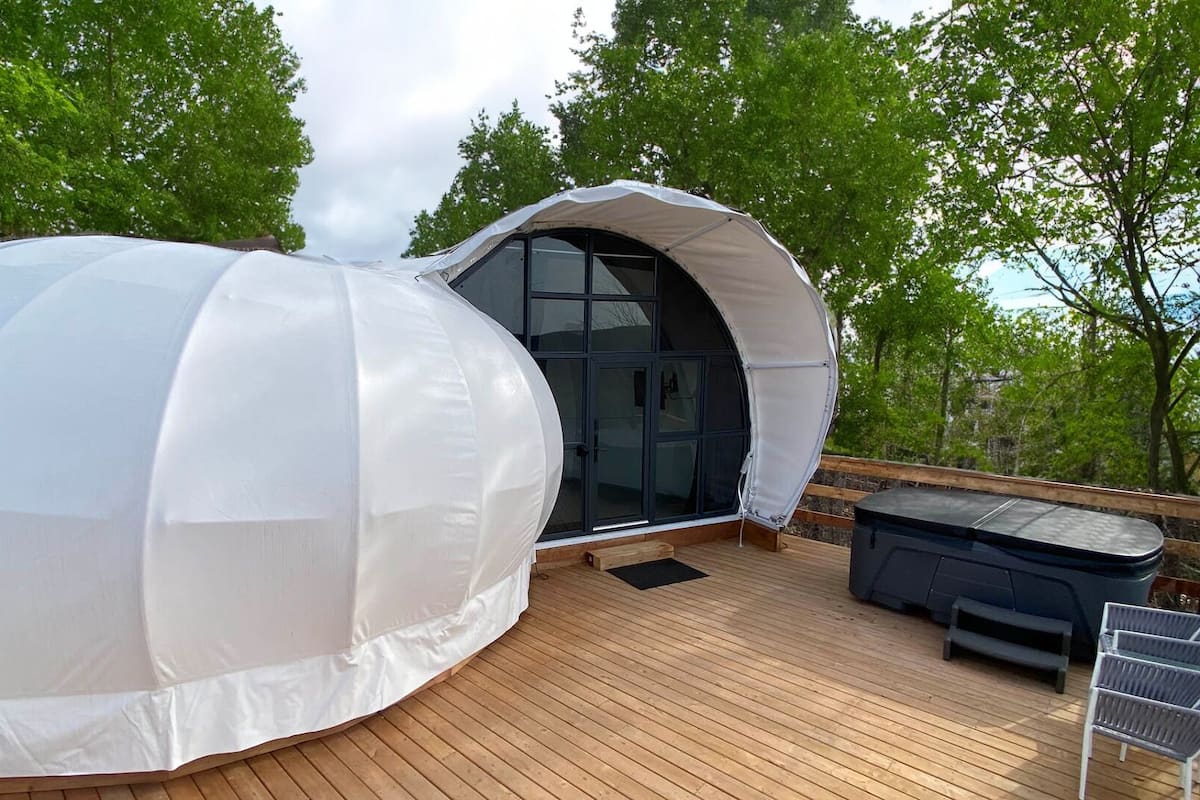 Uma estrutura em forma de cúpula com porta de vidro, deck de madeira e banheira de hidromassagem.