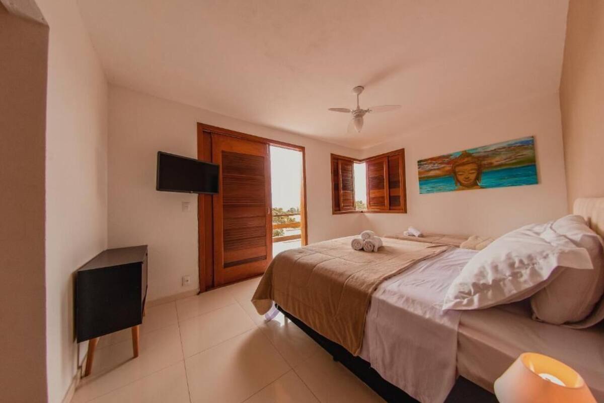 Quarto com cama, televisão, ventoinha no teto, quadro e vista através de uma porta.