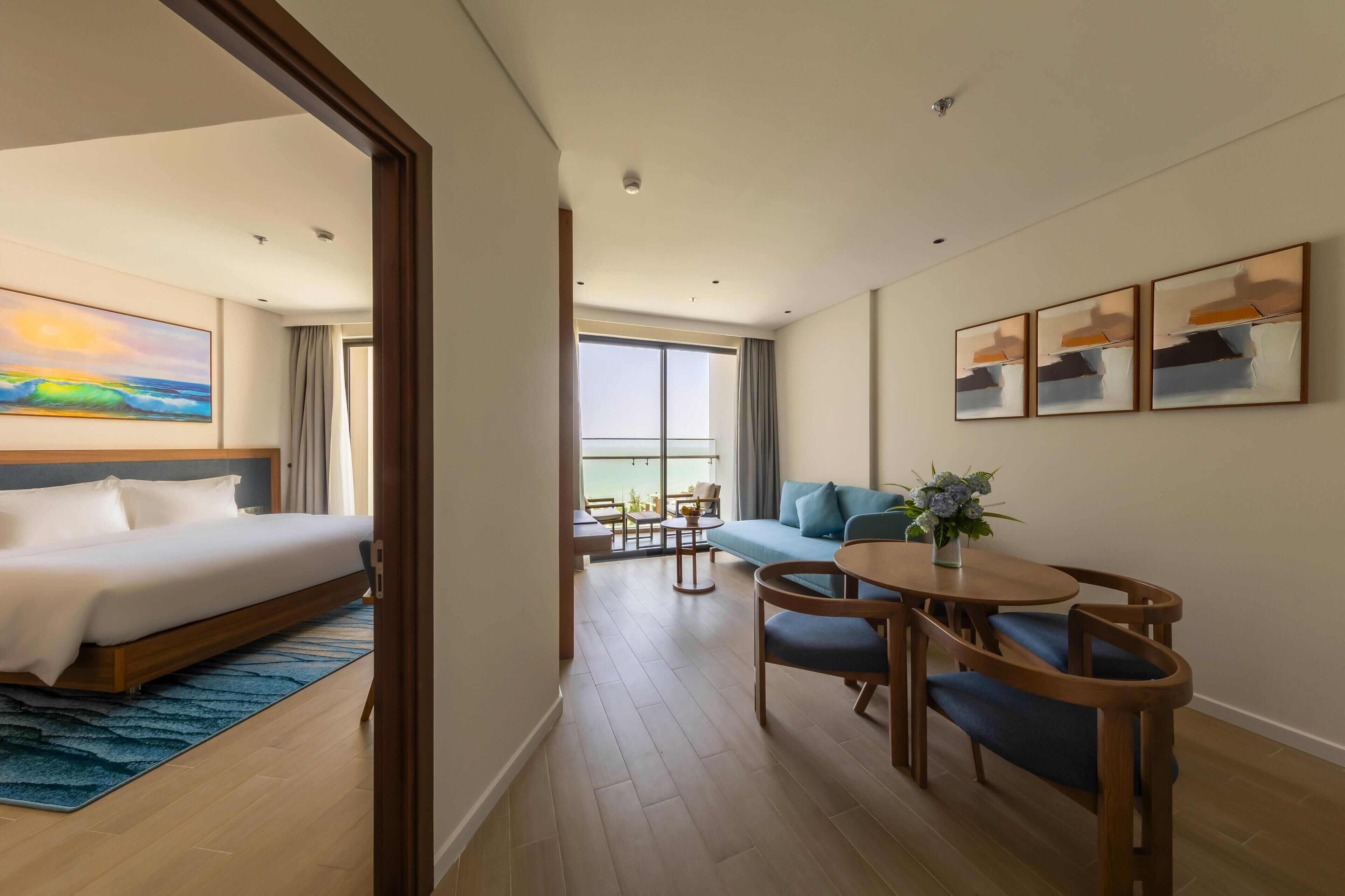Quarto de hotel com cama, sofá, mesa de jantar com cadeiras e obras de arte nas paredes.