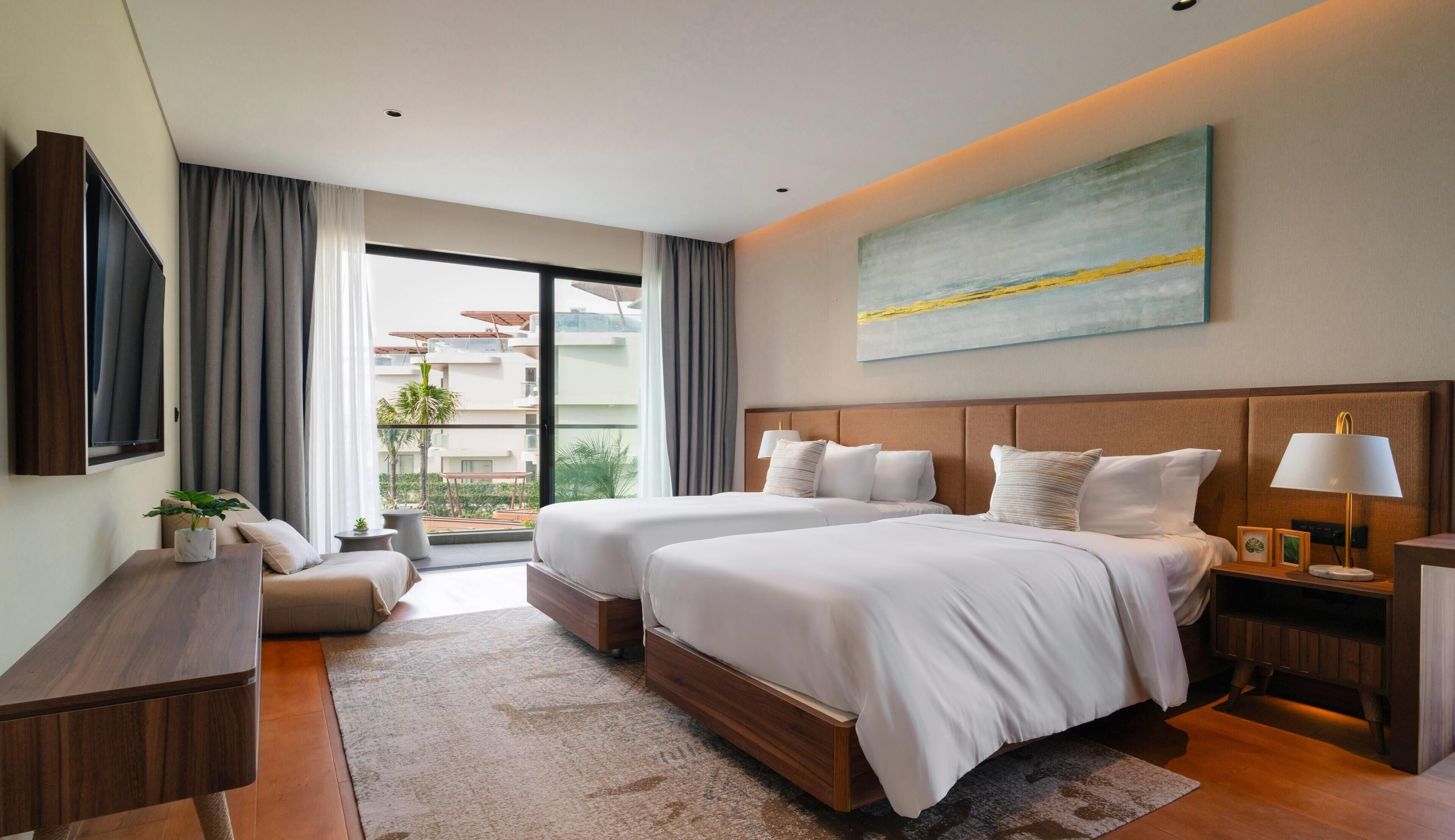Quarto de hotel com duas camas, uma televisão de tela plana, uma escrivaninha e uma varanda com vista.