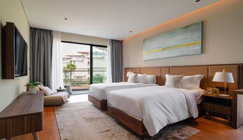 Quarto de hotel com duas camas, uma televisão de tela plana, uma escrivaninha e uma varanda com vista.