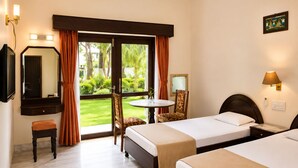 Quarto de hotel com duas camas, uma mesa pequena, uma cadeira, um espelho e uma janela com cortinas.