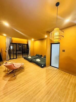 Quarto de hotel moderno com piso de madeira, duas camas, uma cadeira de balanço, uma janela grande e um lustre.