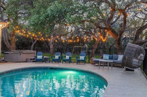 Uma piscina com cadeiras e um sofá, cercada por árvores e luzes de corda.